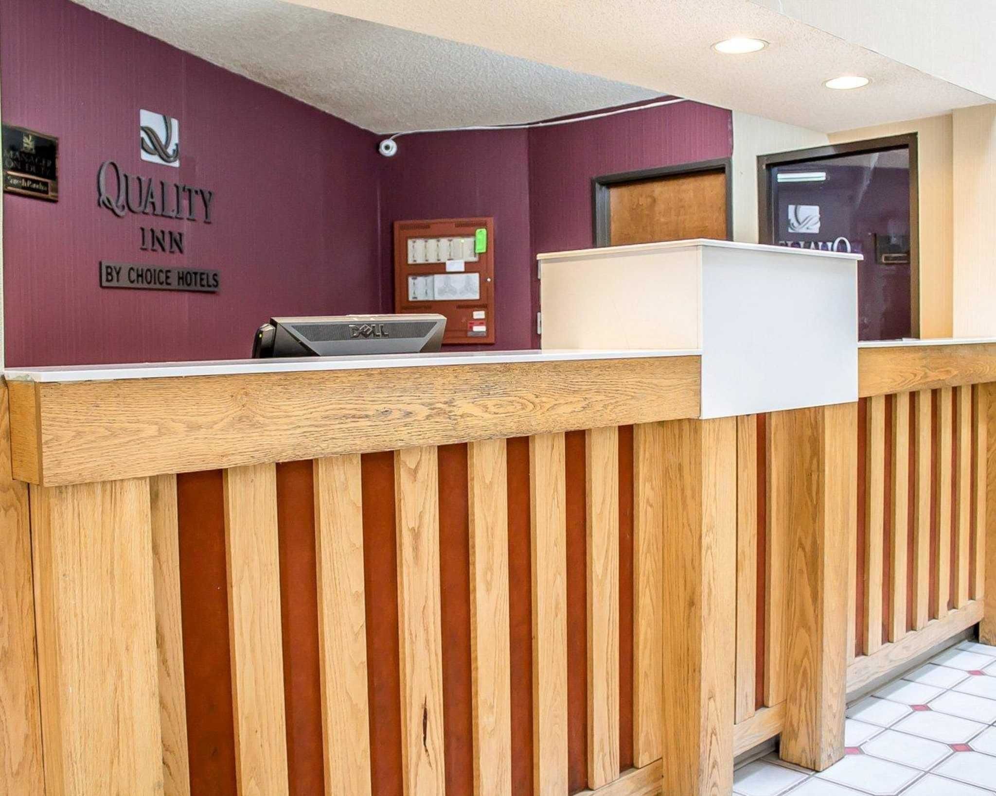 Balcão de recepção de hotel com bancada de madeira e parede vermelha.