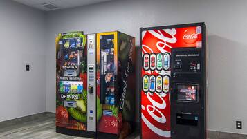 Três máquinas de venda automática numa sala com chão ladrilhado e paredes brancas.