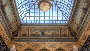 Um interior imponente com cúpula de vidro, afrescos elaborados e uma escadaria de mármore.