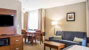 Quarto de hotel com televisão de tela plana, mesa de jantar com cadeiras, sofá, luminária e um quadro na parede.