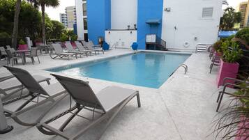 Piscina com espreguiçadeiras e deck de concreto.