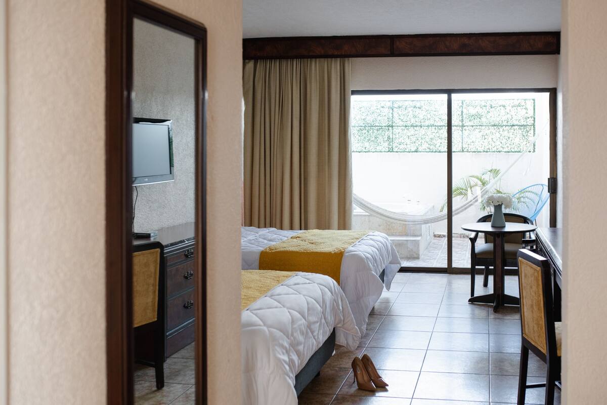 Quarto de hotel com duas camas, televisão, mesa de trabalho com cadeira e varanda com vista.