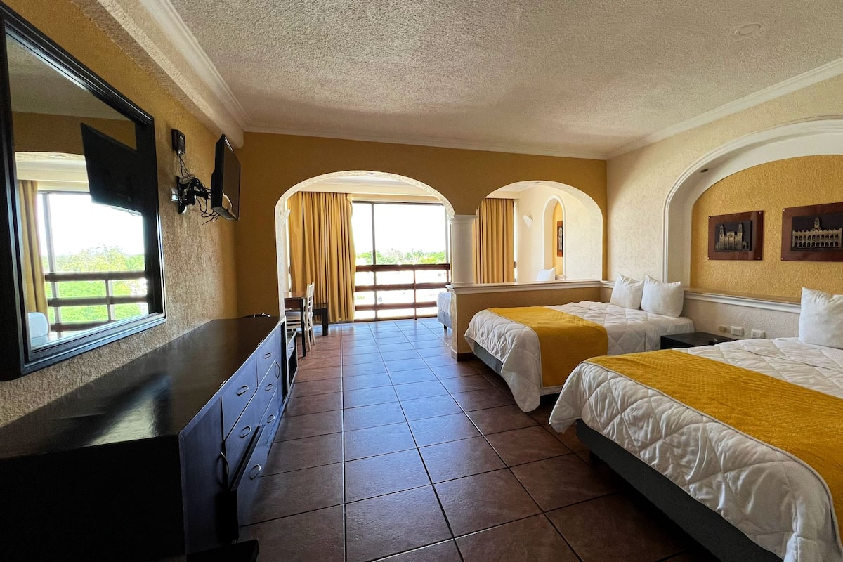 Quarto de hotel com duas camas, uma escrivaninha e uma janela grande.