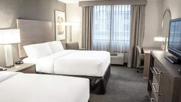Quarto de hotel com duas camas, uma escrivaninha, televisão e uma janela grande com cortinas.