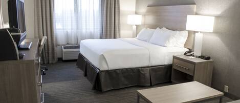 Quarto de hotel com cama, mesas de cabeceira, escrivaninha com cadeira, televisão e ar condicionado.