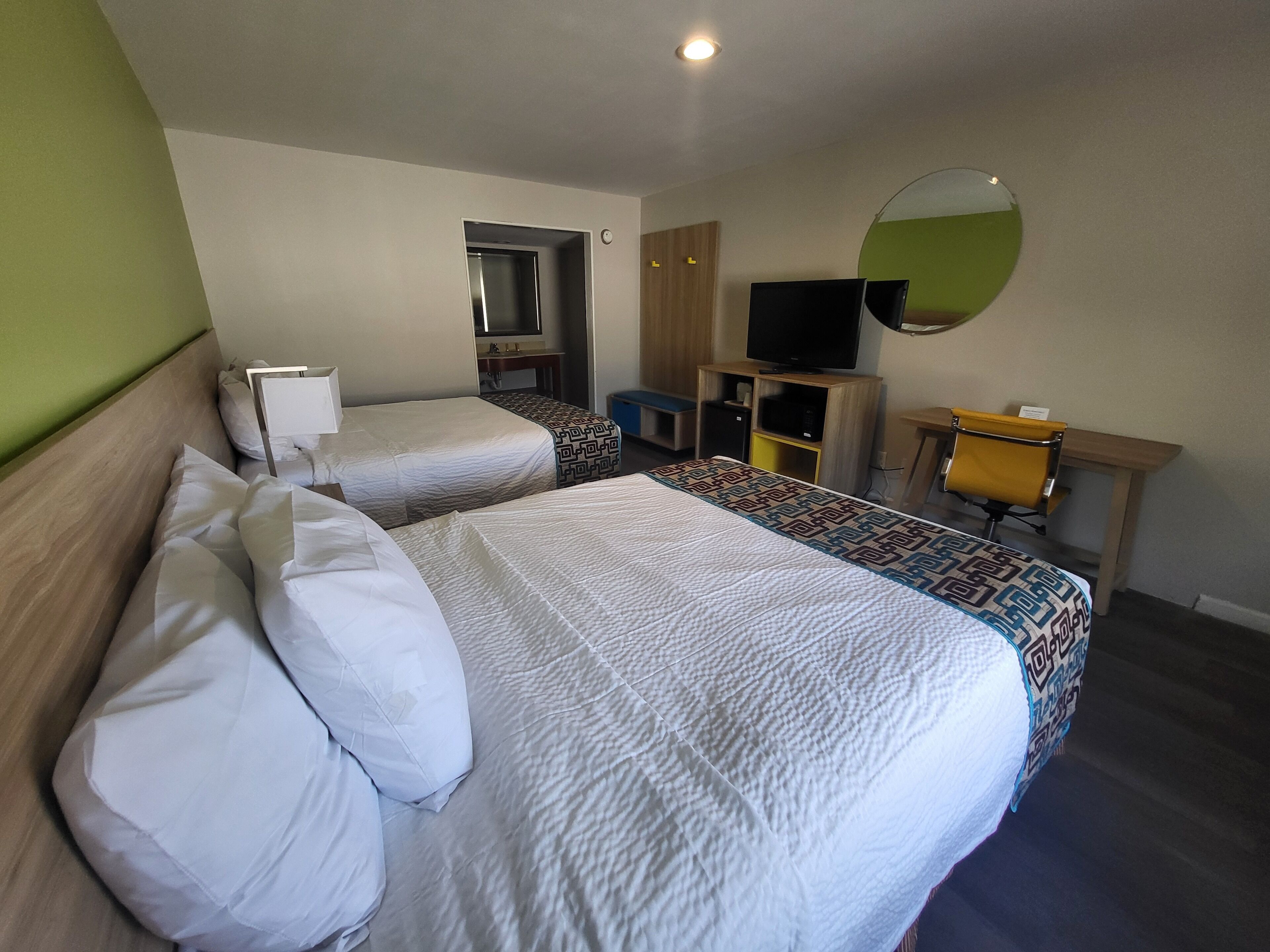 Quarto de hotel com duas camas, televisão, escrivaninha e espelho.