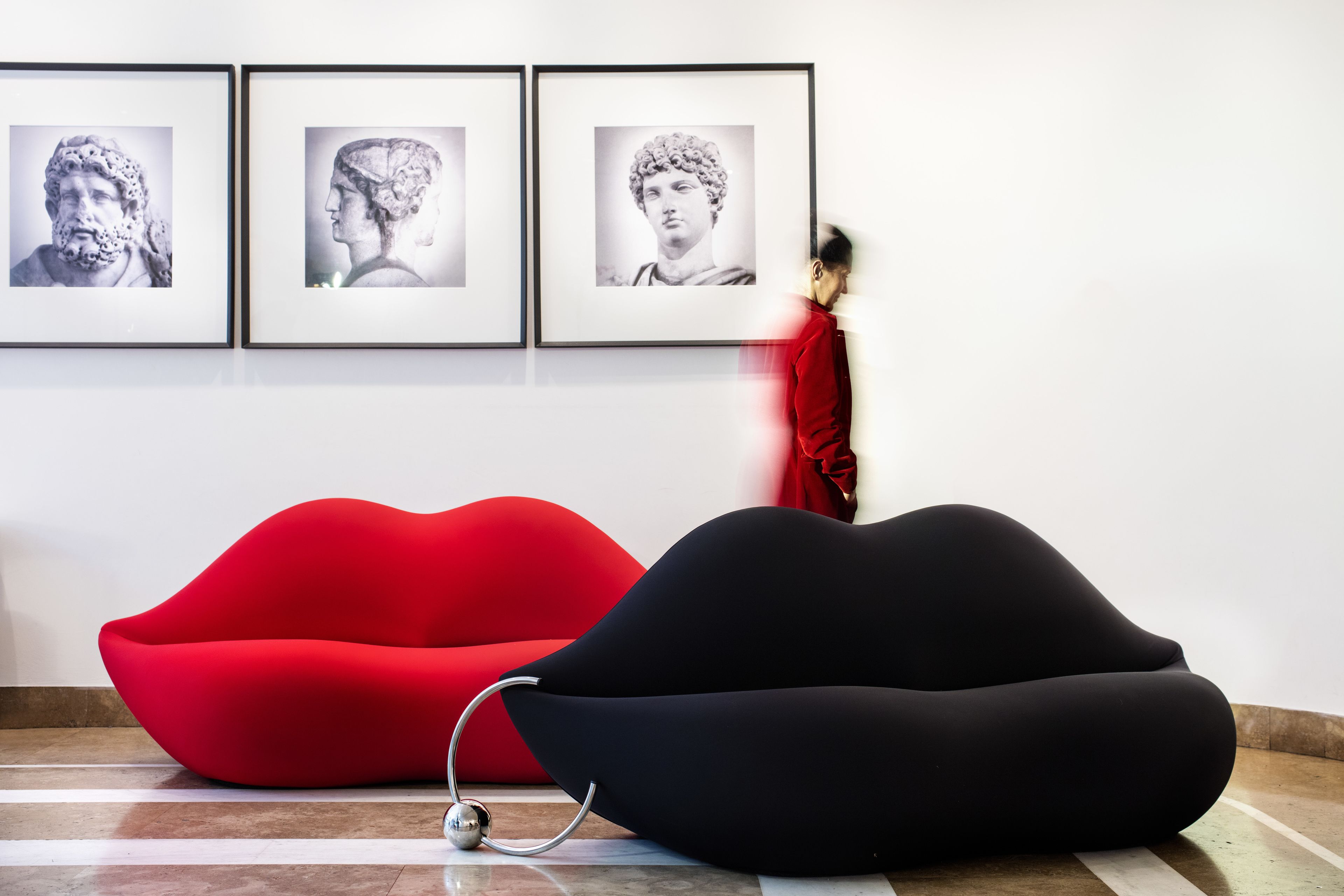 Um interior moderno com uma poltrona de tecido vermelha e preta, piso de mármore e obras de arte emolduradas na parede.