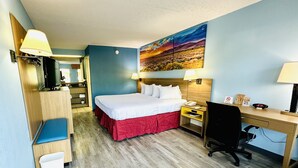 Quarto de hotel com cama, escrivaninha, cadeira e um quadro na parede.