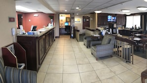 Um hall de hotel com uma mesa de recepção, área de estar e uma kitchenette.