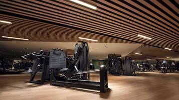 Uma academia com diversos equipamentos de exercícios, piso de madeira e teto com luminárias lineares.