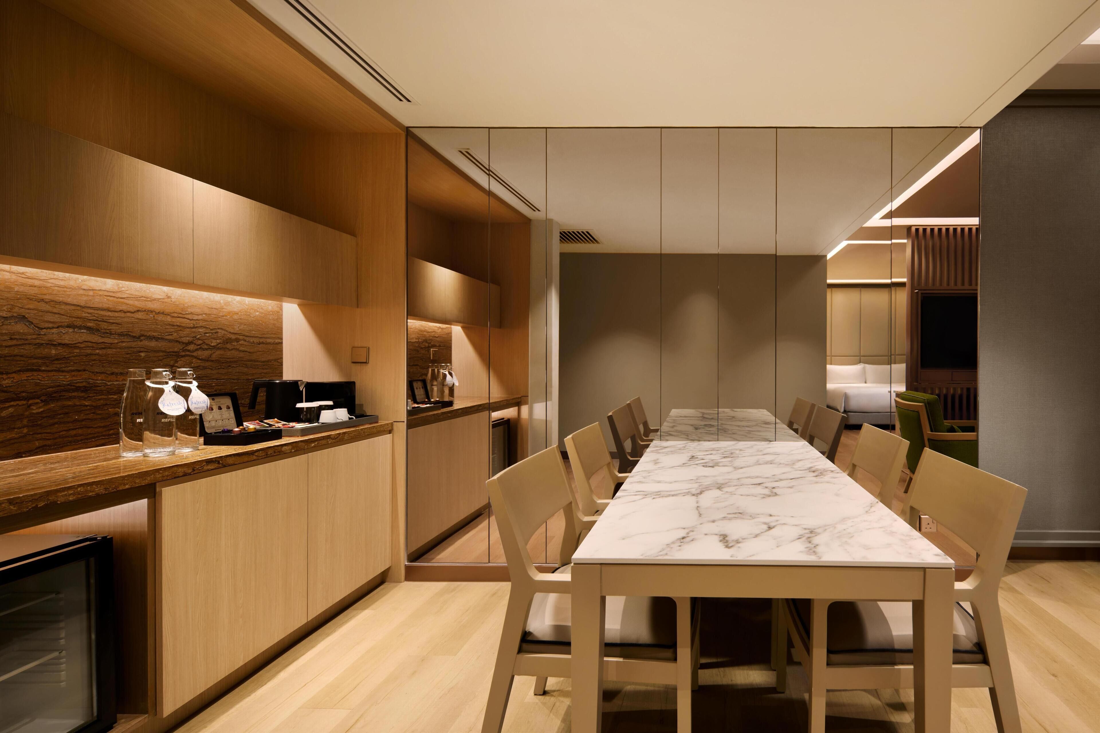 Uma sala de jantar moderna com mesa de mármore e cadeiras de madeira, bancada de cozinha com eletrodomésticos e um espaço de estar com sofá e poltronas.