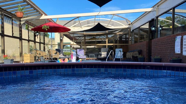 Piscina com cobertura de vidro, área de estar ao ar livre e parede de tijolos.