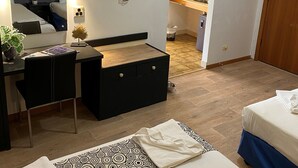 Quarto de hotel com cama, escrivaninha, cadeira, televisão, ar condicionado e cozinha compacta.
