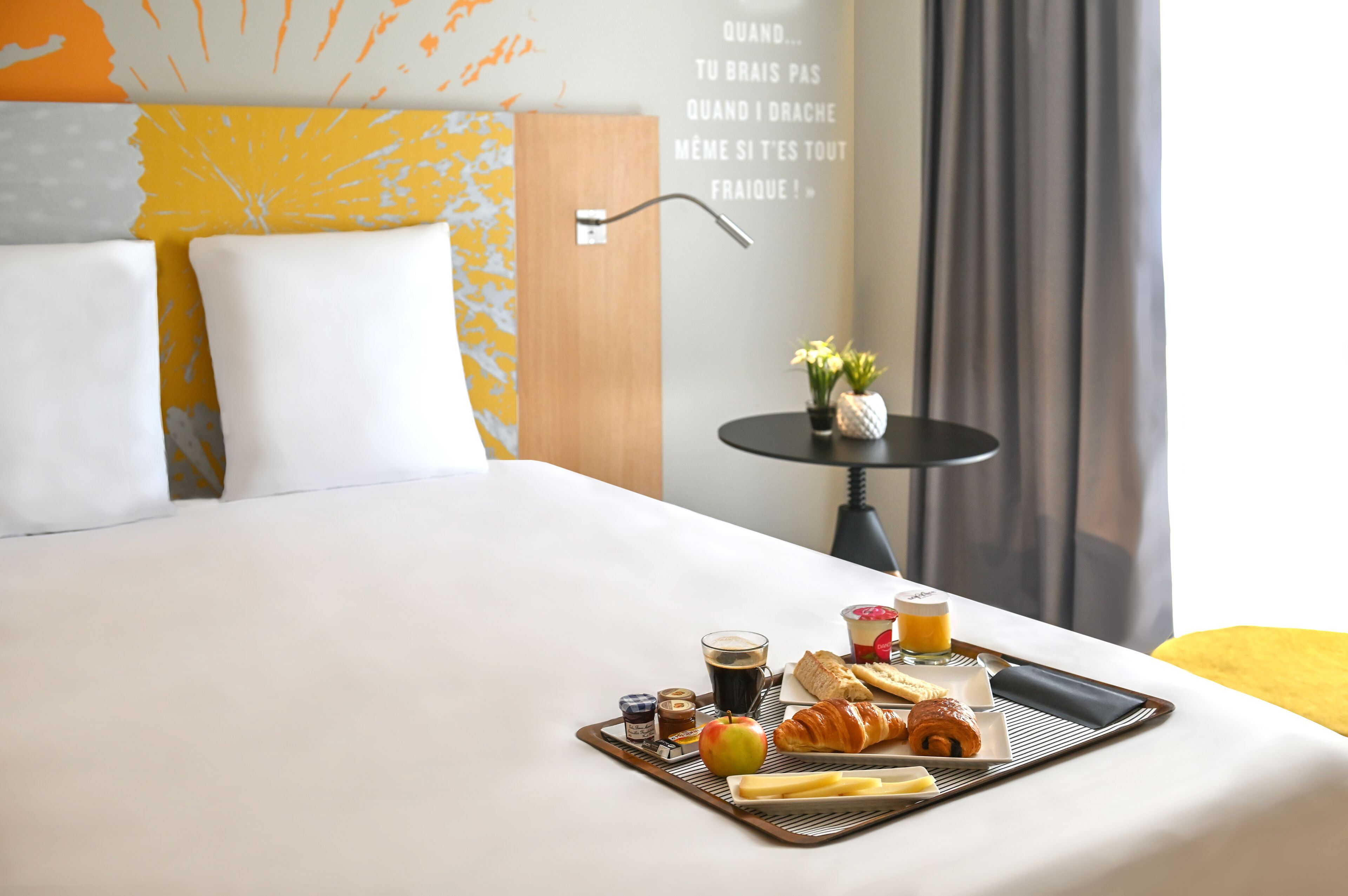 Cama arrumada com bandeja de café da manhã, incluindo croissants, uma maçã e um copo de suco.
