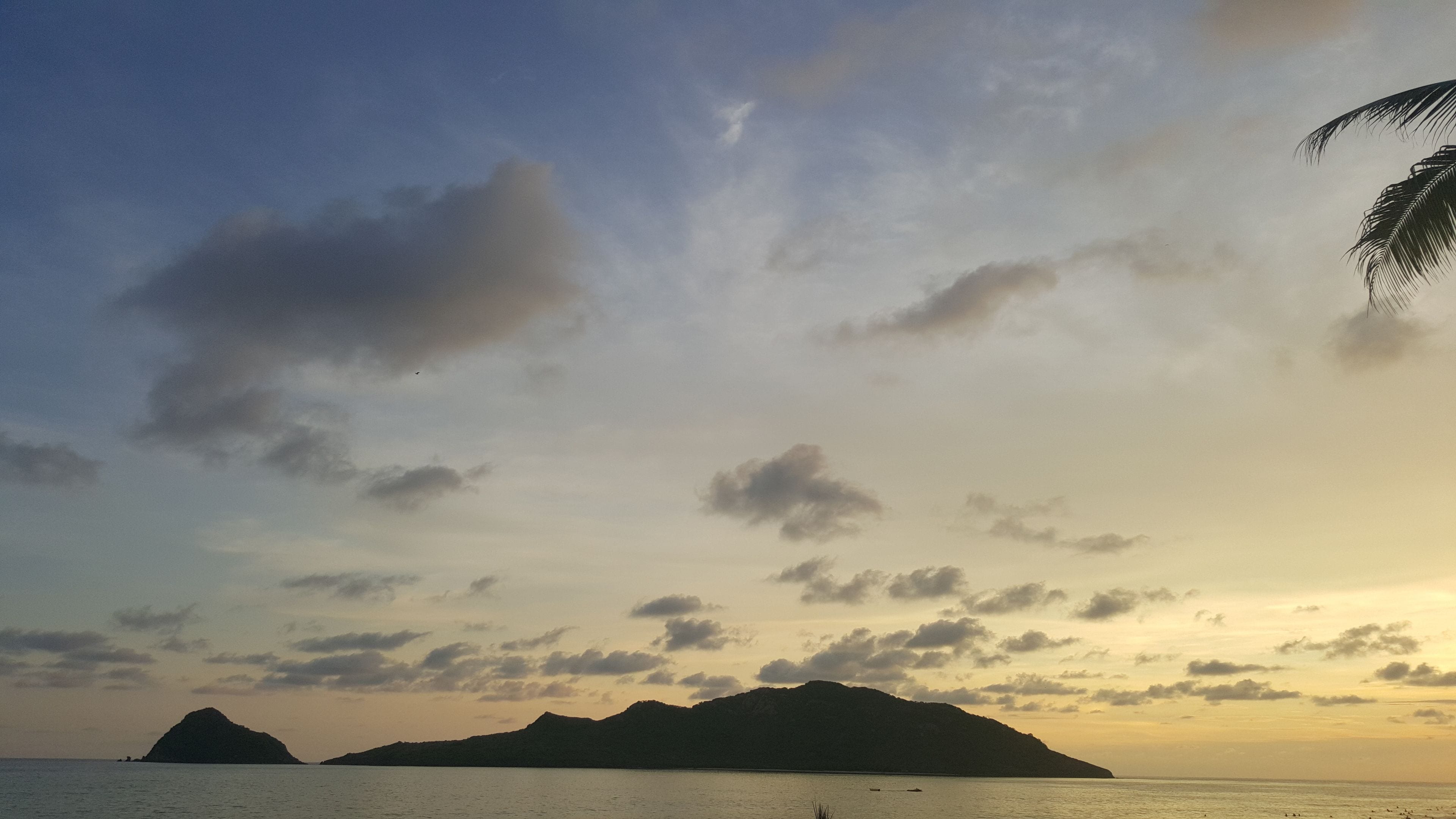 Paisagem costeira com mar calmo e ilhas ao longe, sob um céu parcialmente nublado.