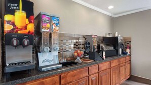 Uma estação de bebidas de serviço, com opções de suco de laranja e suco de maçã, um dispensador de cereais e uma cafeteira.