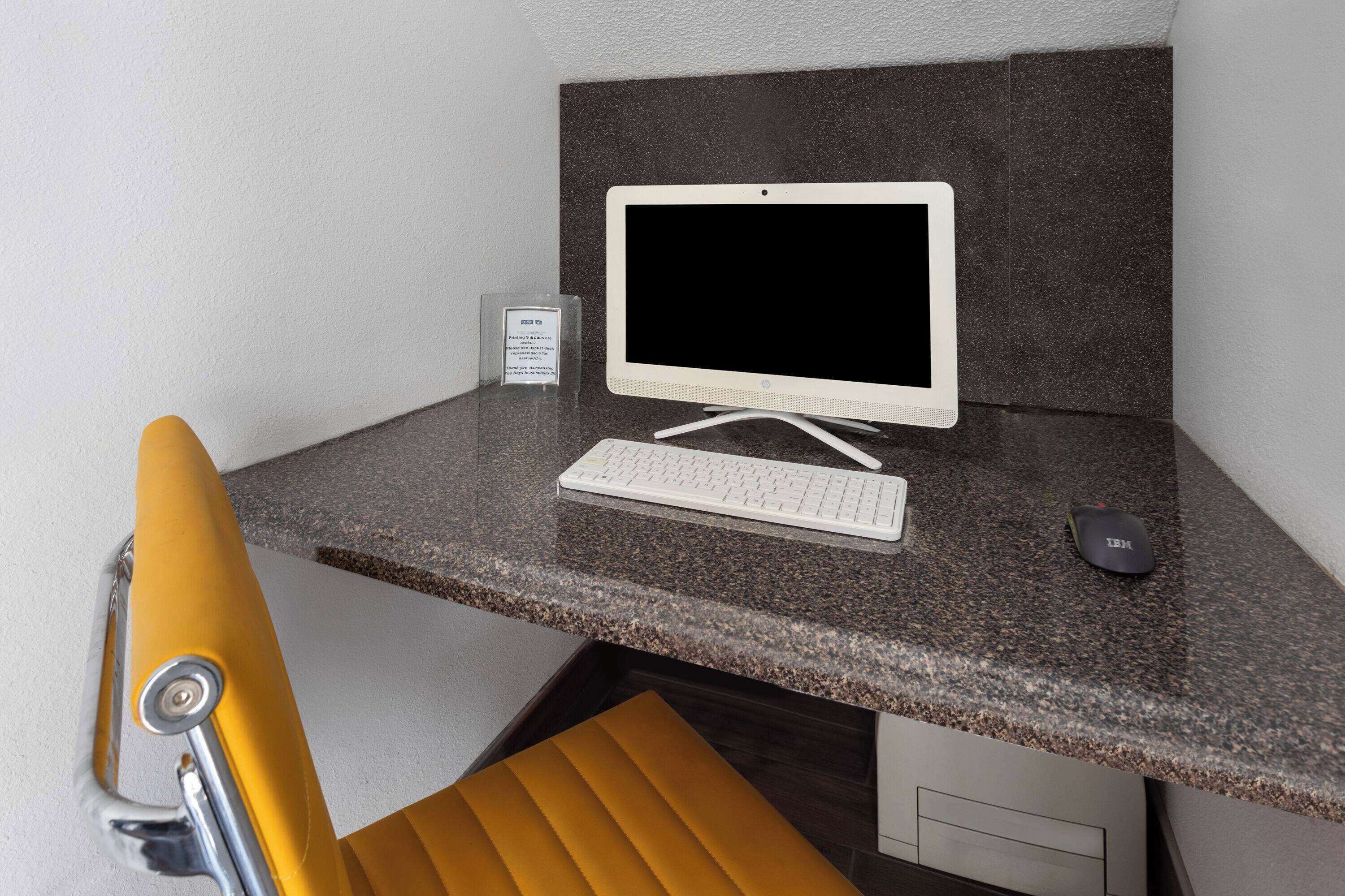 Um espaço de trabalho moderno com um computador de mesa, teclado, rato e uma cadeira amarela.