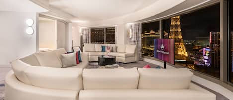 Uma sala de estar moderna com uma janela ampla que oferece vista da cidade, um conjunto de sofás e uma mesa de centro.