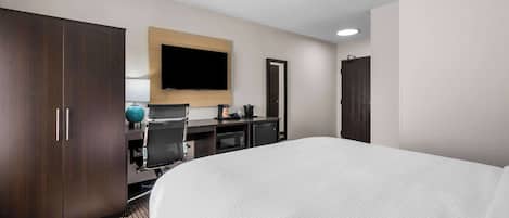 Quarto de hotel com uma cama grande, uma escrivaninha com computador, uma televisão de tela plana e um guarda-roupa.