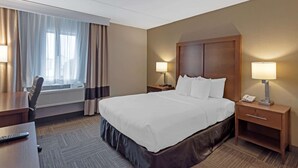 Quarto de hotel com uma cama grande, duas mesas de cabeceira com abajures, uma escrivaninha com cadeira e uma janela com cortinas.