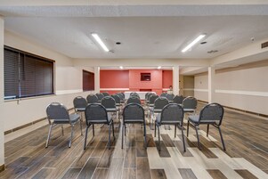 Uma sala de conferências com fileiras de cadeiras, uma parede com detalhes vermelhos e piso ladrilhado.