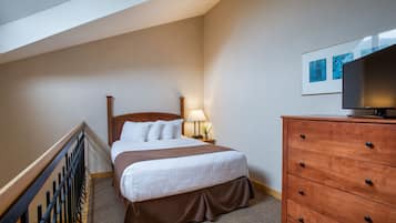 Quarto de hotel com cama, penteadeira, televisão e abajur.