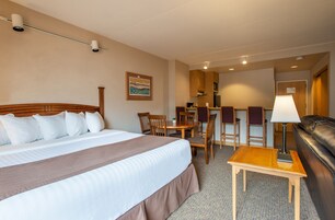 Quarto de hotel com uma cama grande, uma mesa de madeira, um sofá e uma área de cozinha compacta.