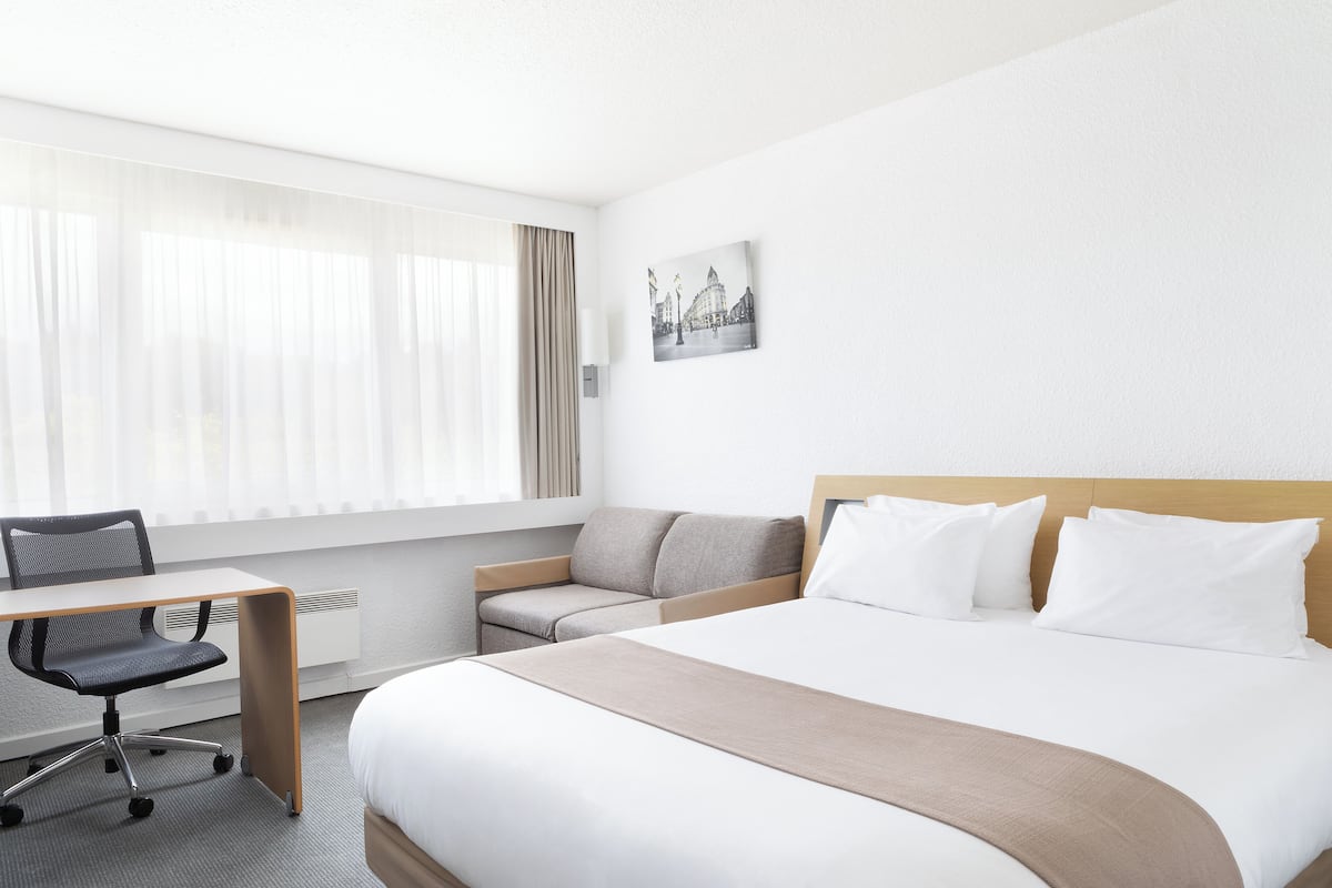Quarto de hotel com cama, escrivaninha, cadeira e sofá.