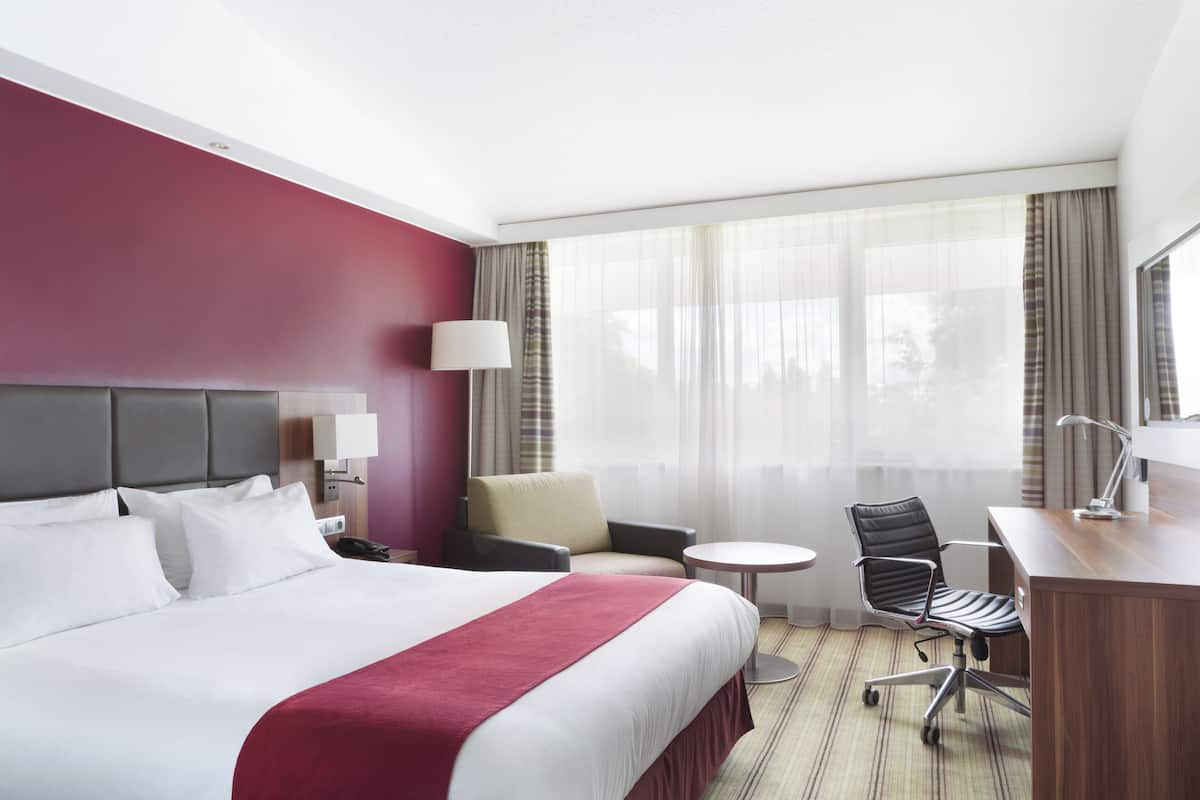Quarto de hotel com uma cama grande, uma mesa, uma cadeira, uma pequena mesa e um abajur.