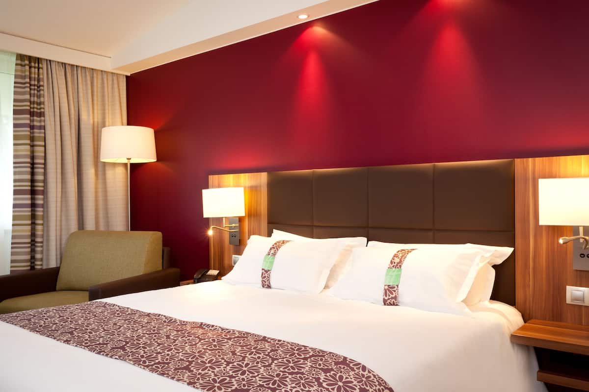 Quarto de hotel com uma cama grande, uma cadeira, uma escrivaninha e um abajur.