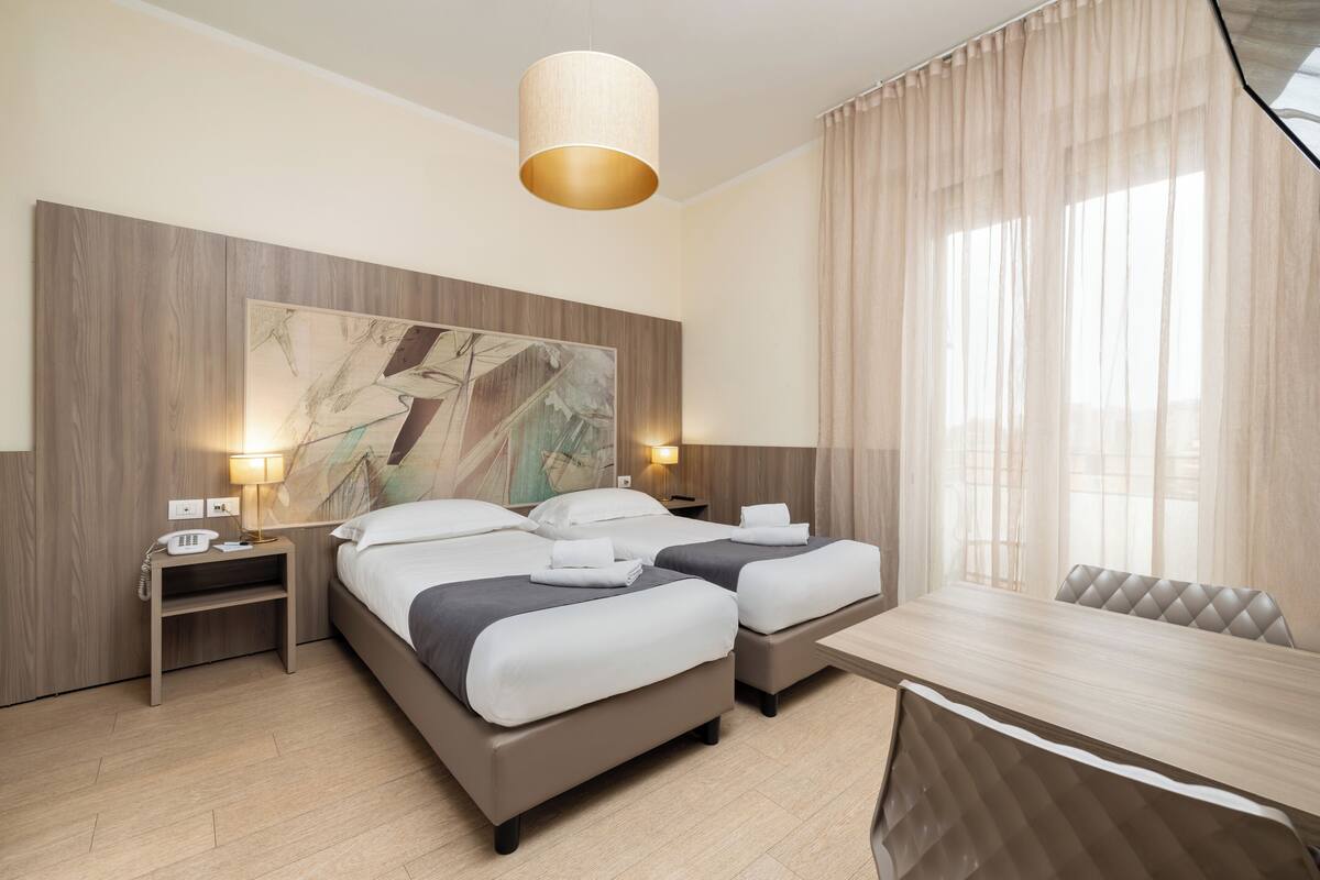 Quarto de hotel com duas camas, uma escrivaninha e uma grande pintura abstrata na parede.
