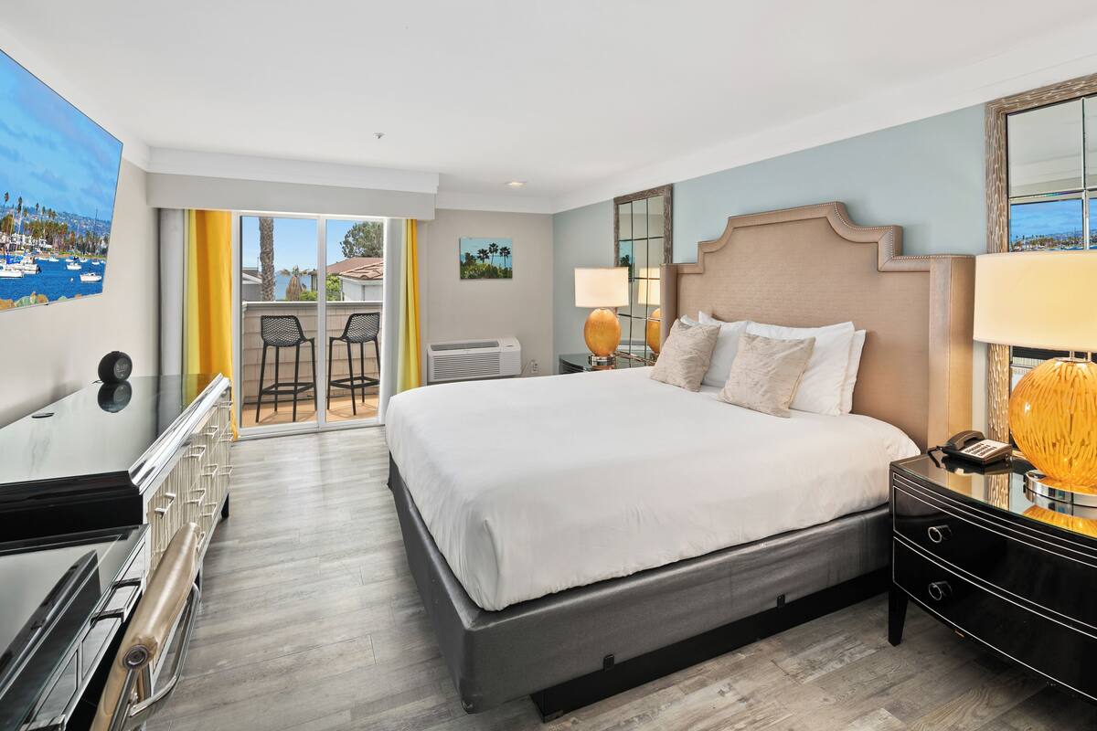 Quarto de hotel com uma cama grande, uma escrivaninha, uma cadeira e uma varanda com vista para o mar.