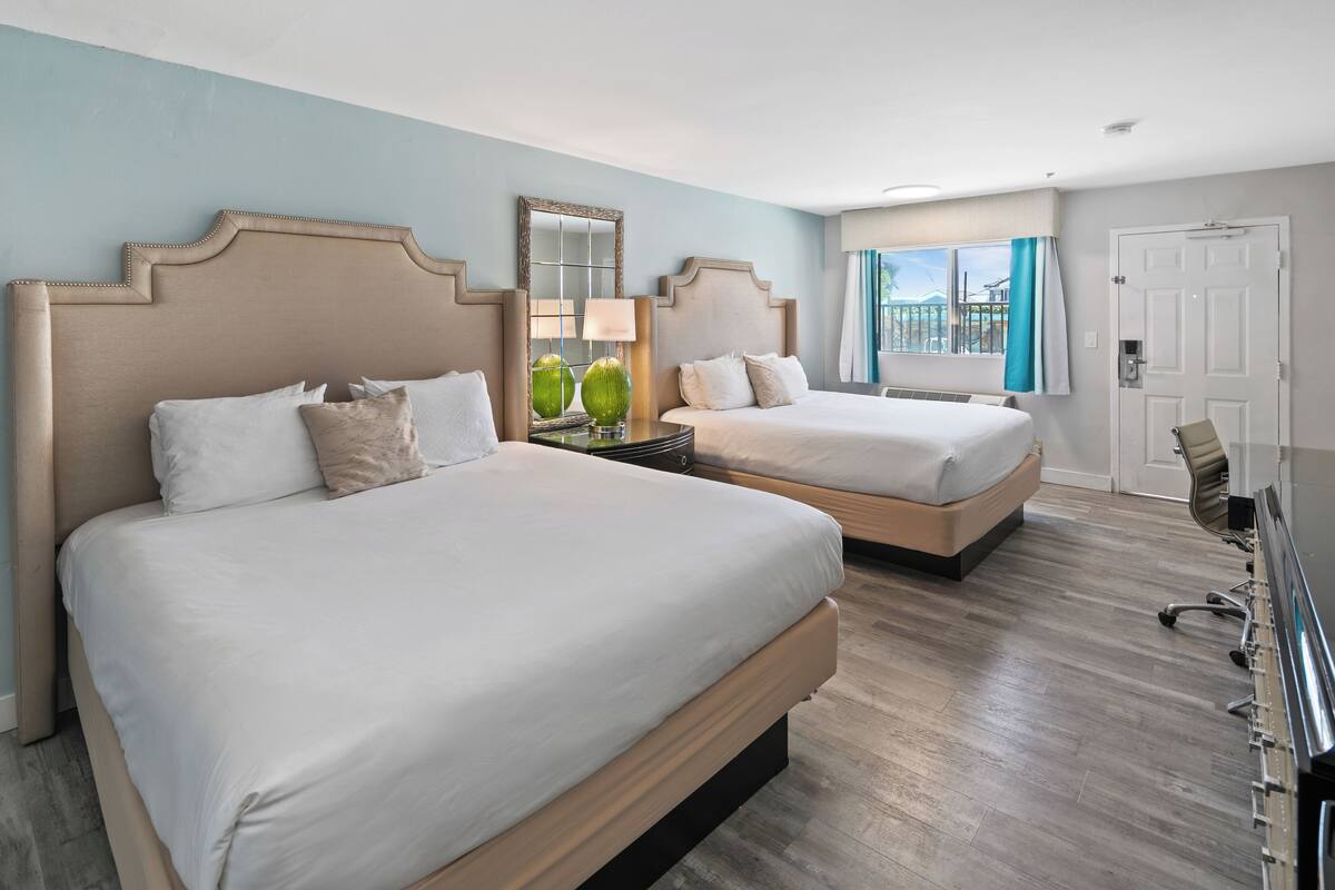 Quarto de hotel com duas camas, um espelho grande, uma mesa de cabeceira e vista para o exterior.