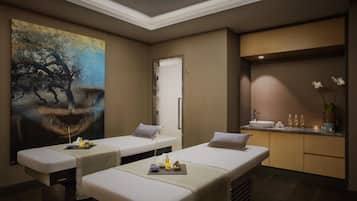 Sala de spa com duas macas de tratamento, uma pintura grande, uma pia e uma pequena planta.