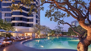 Um hotel com piscina, espreguiçadeiras e uma grande árvore.
