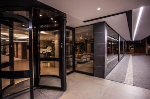 Um saguão de hotel com porta giratória, área de estar com sofás e balcão de recepção.