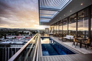 Uma área de piscina moderna ao ar livre, com guarda-corpo de vidro, assentos e vista para a paisagem circundante.