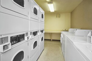Uma lavanderia com várias máquinas de lavar e secar empilhadas, um balcão com pia e um luminar fluorescente no teto.