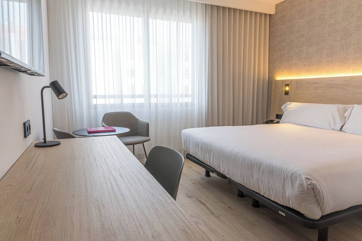 Quarto de hotel com cama, escrivaninha, cadeira, mesa e televisão.