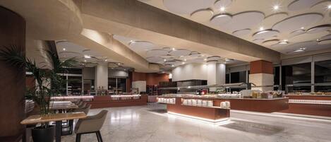 Um hall amplo com design moderno, com uma ilha central com pratos expostos, uma área de estar com mesa e cadeiras, e um teto único com luminárias circulares.