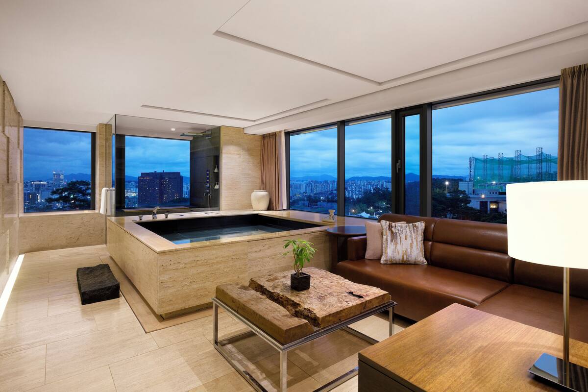 Quarto de hotel moderno com uma banheira grande, um sofá, uma mesa de centro e vista para a cidade.