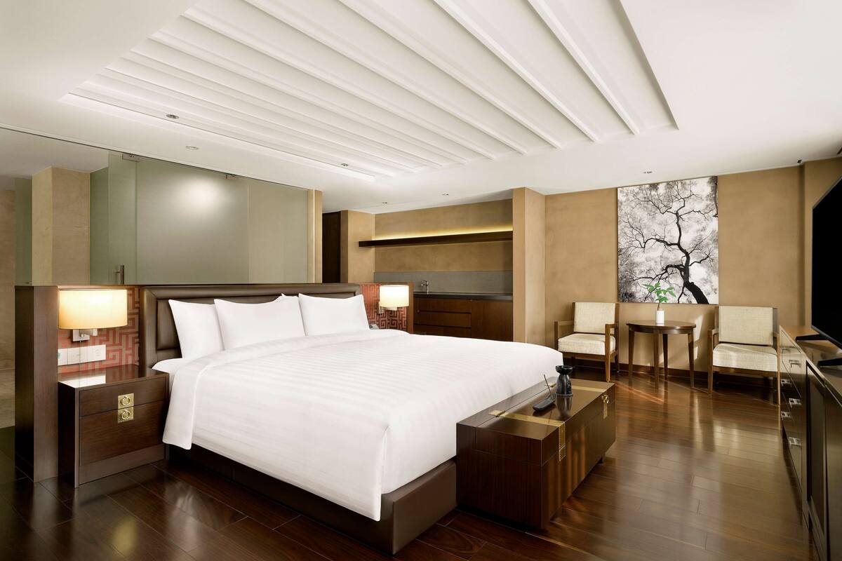 Quarto de hotel moderno com uma cama grande, uma escrivaninha, uma cadeira e um quadro na parede.