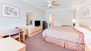 Quarto de hotel com cama, escrivaninha, cadeira, televisão e ventoinha no teto.
