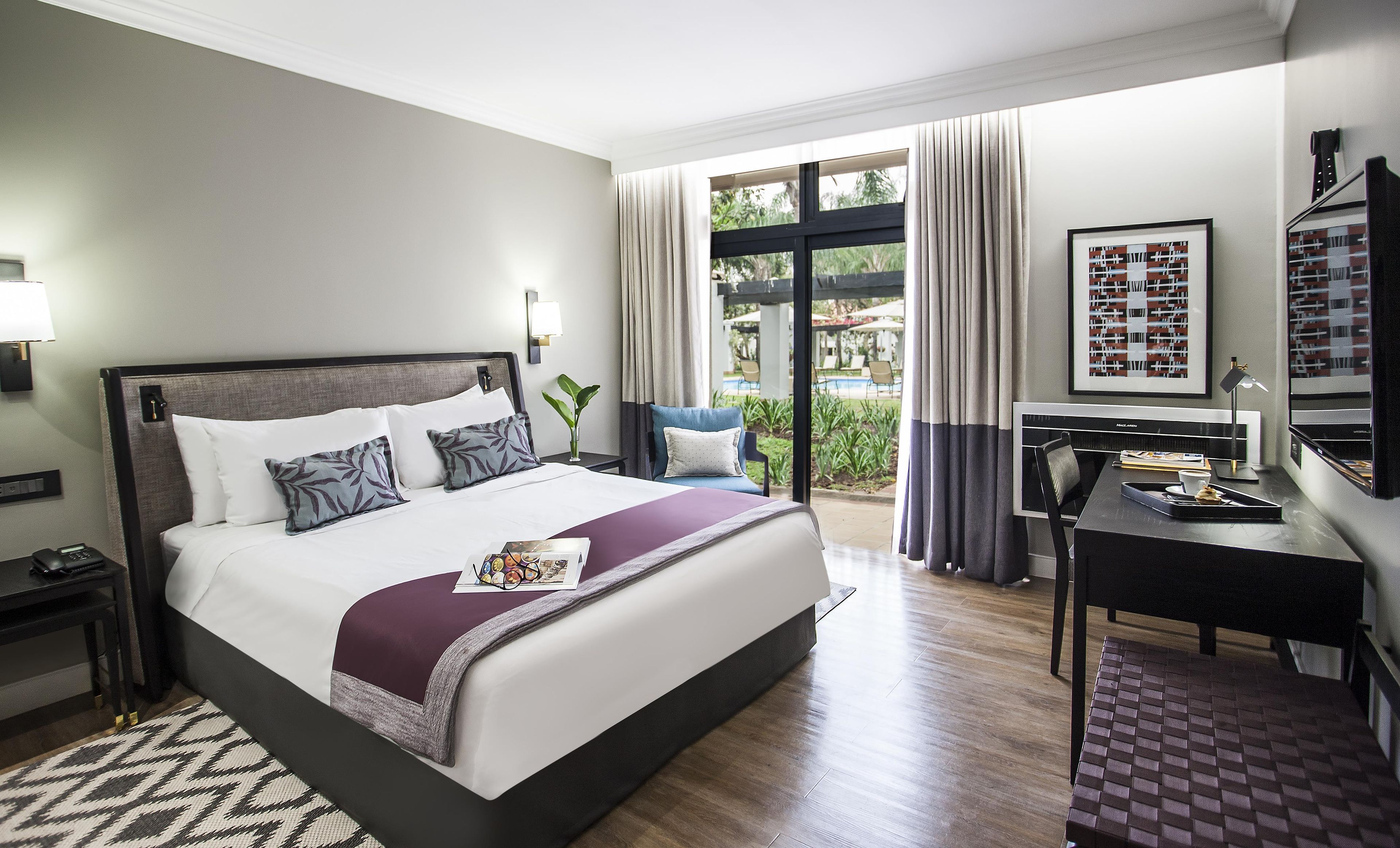 Quarto de hotel com cama grande, escrivaninha, cadeira e vista para o exterior.