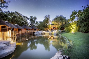 Um ambiente tranquilo ao ar livre com um lago, construções com telhado de palha e um jardim bem cuidado.