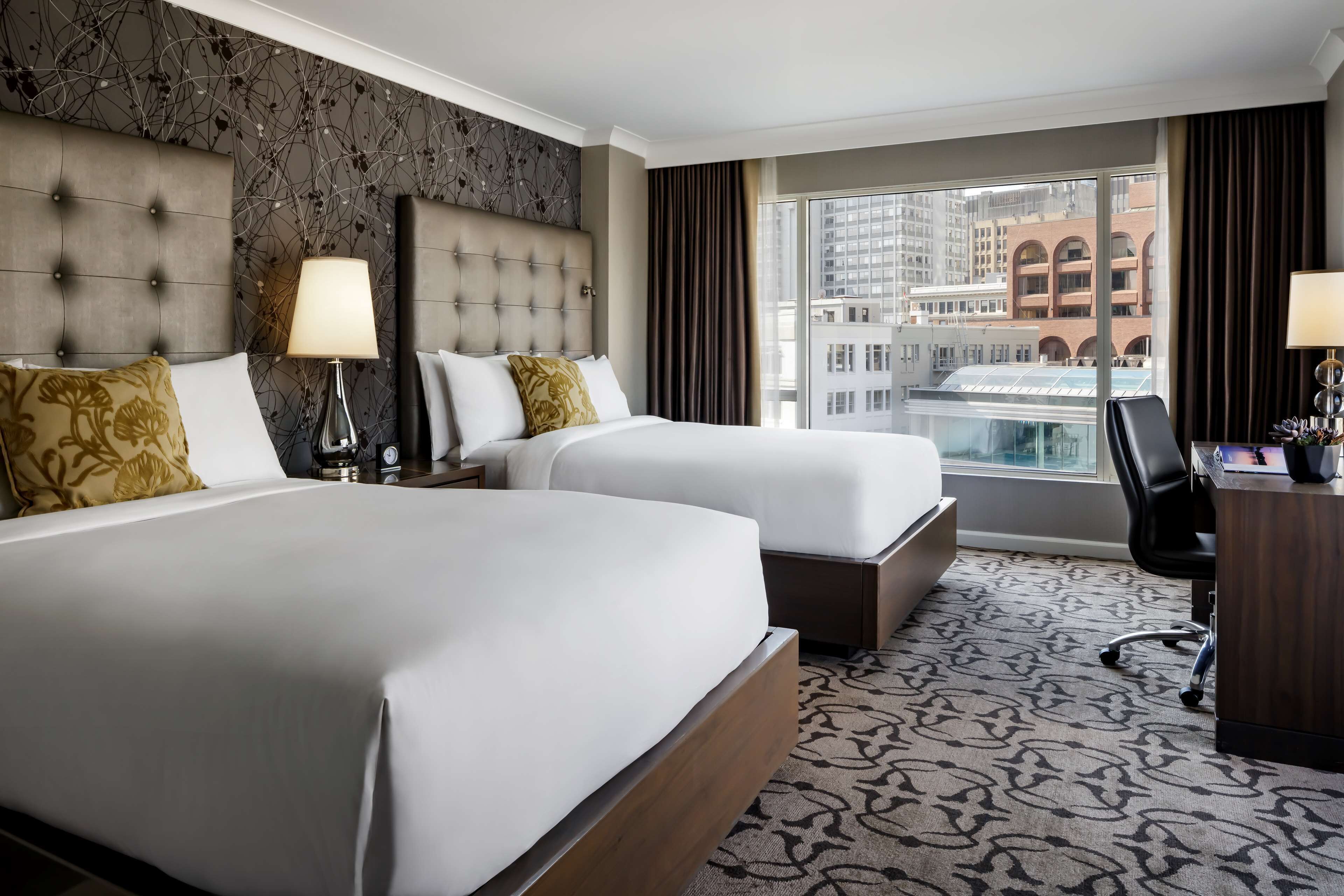 Quarto de hotel com duas camas, uma escrivaninha e vista para a cidade.