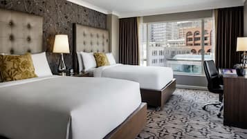 Quarto de hotel com duas camas, uma escrivaninha e vista para a cidade.
