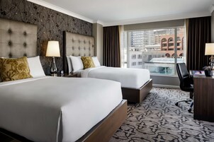 Quarto de hotel com duas camas, uma escrivaninha e vista para a cidade.
