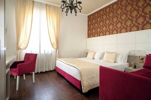 Quarto de hotel com cama, escrivaninha, cadeira e mesa de cabeceira.