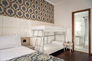 Quarto de hotel com beliche, mesa de cabeceira com abajur, pequena mesa de cabeceira com um pote de vidro e banheiro com box de vidro.